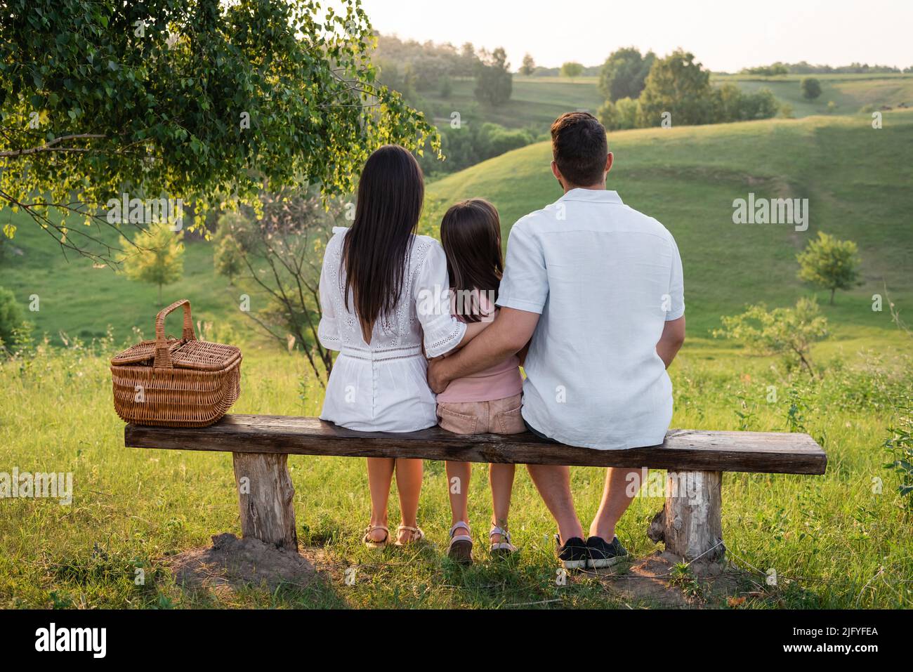 back view of family sitting on bench near wicker basket in front on ...