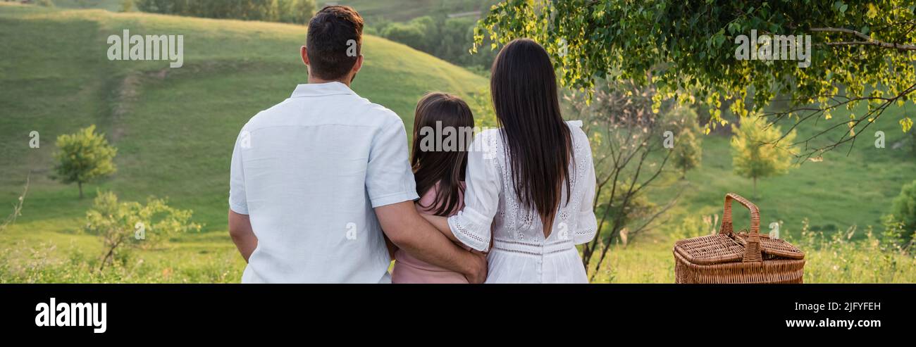 back view of family sitting in front of scenic landscape in countryside ...