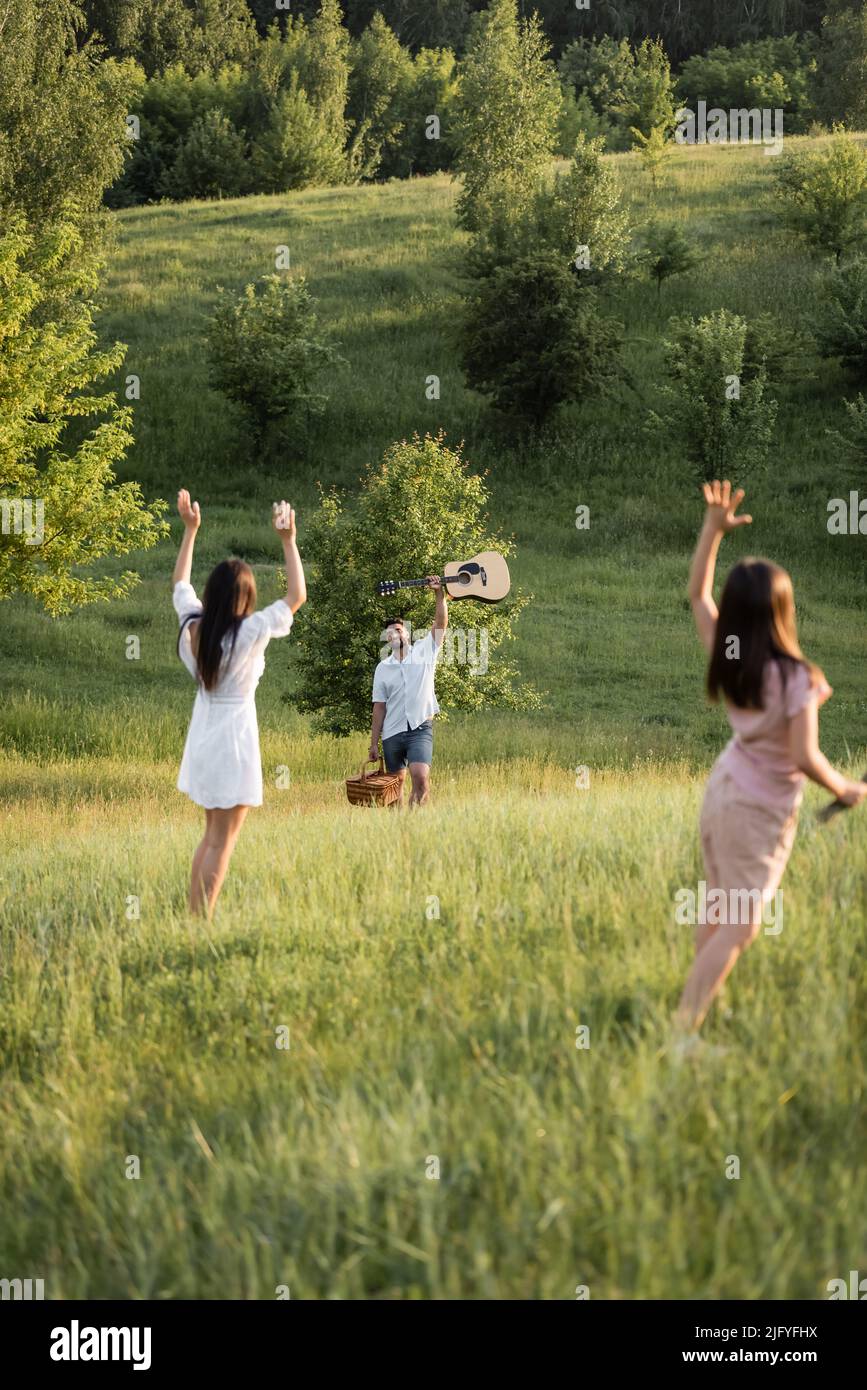 mom and daughter waving hands to man with guitar on picturesque slope ...