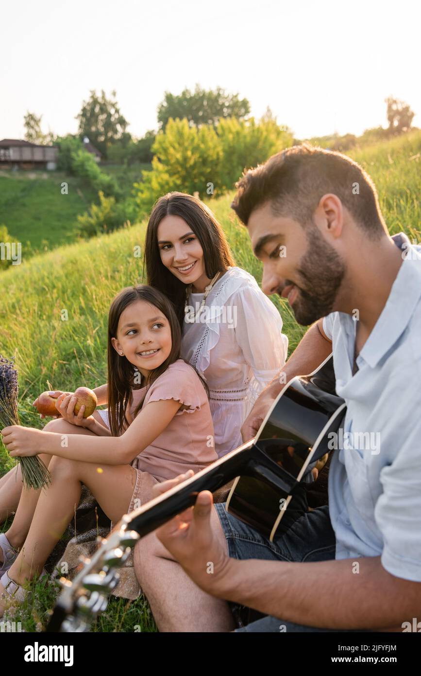 smiling woman with child listening father playing acoustic guitar ...