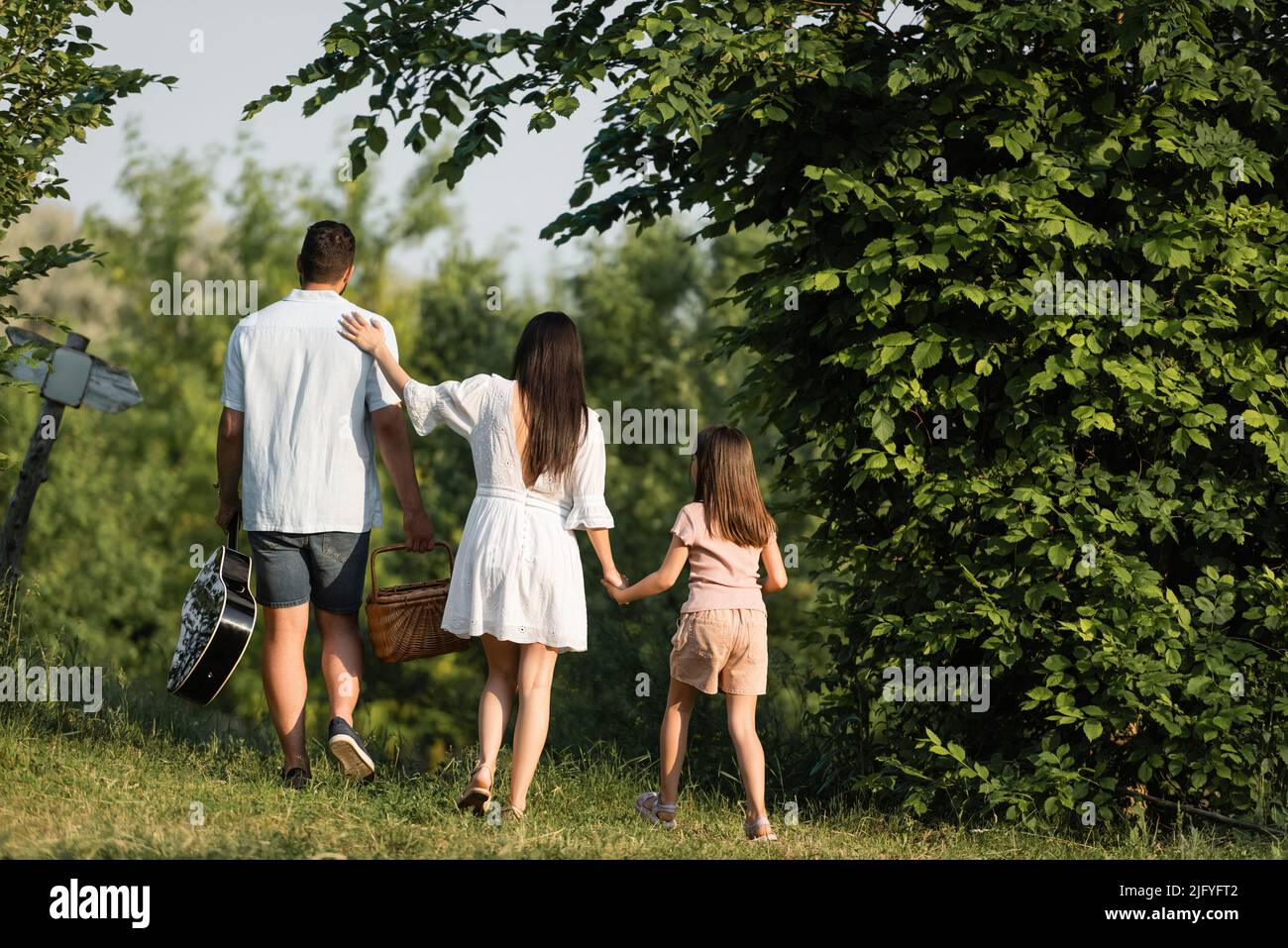 back view of man with wicker basket and acoustic guitar walking with ...