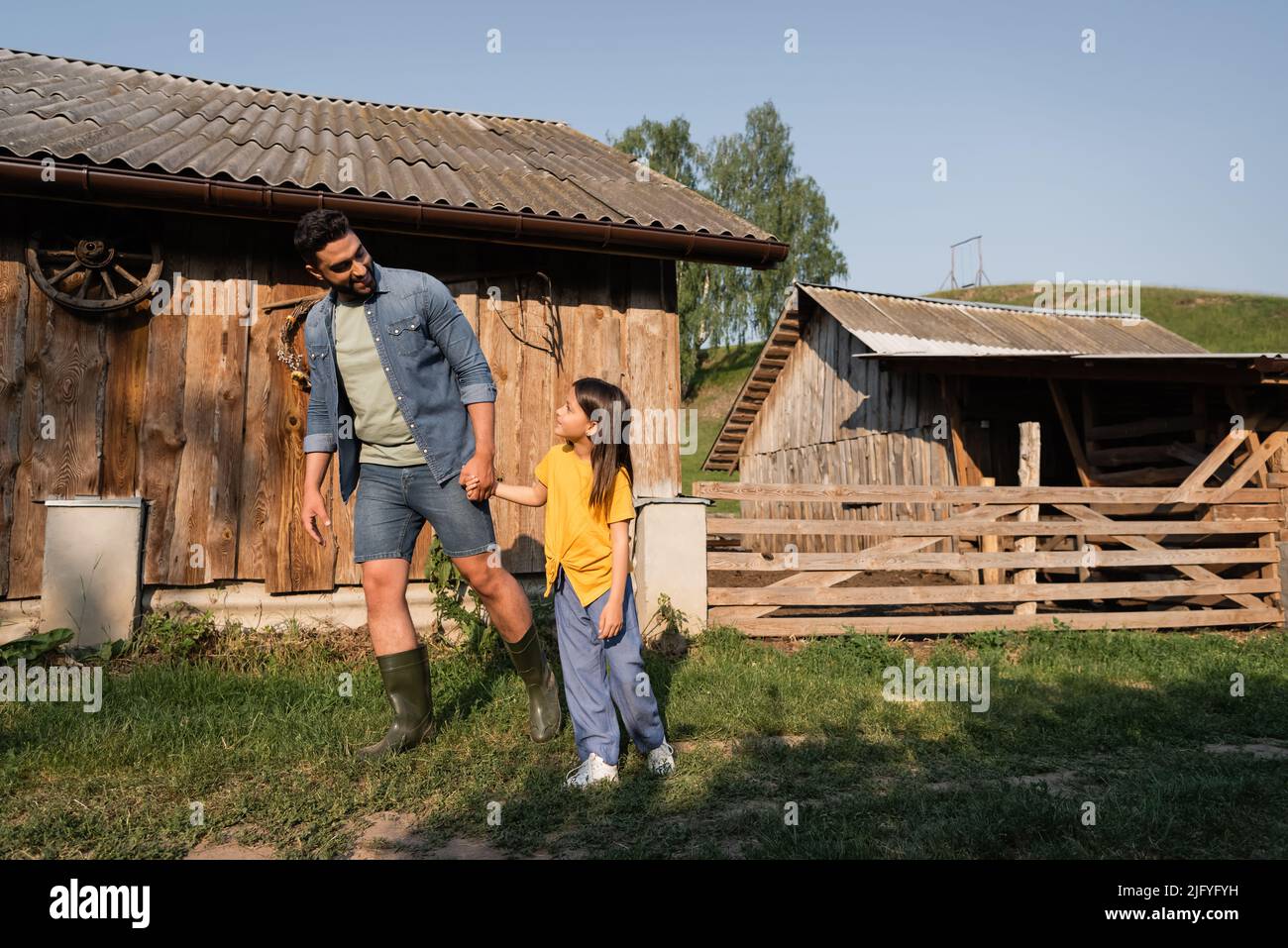 full length of father and daughter holding hands while walking on farm ...