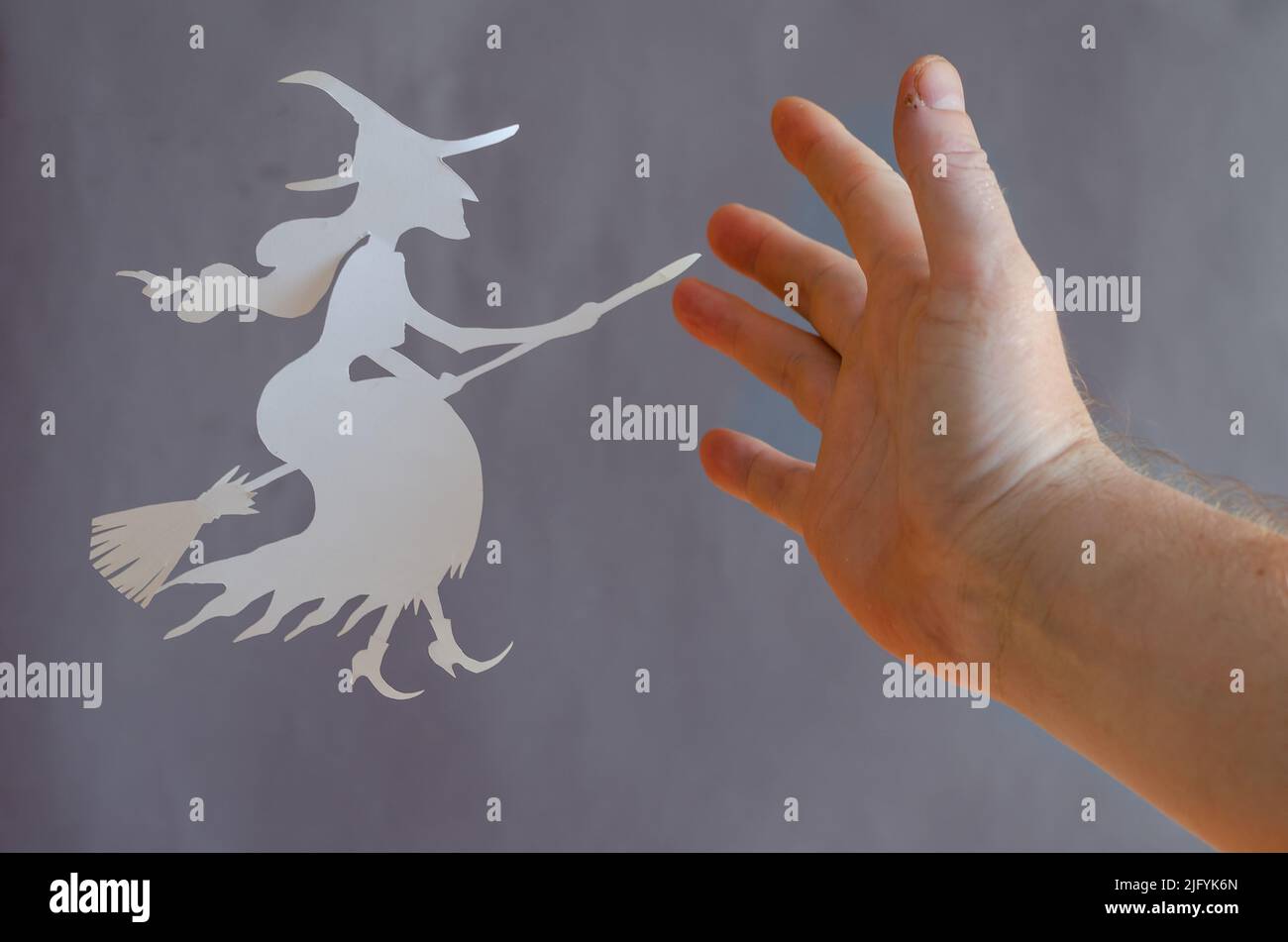 A man stops a flying witch on a broomstick with his hand. White paper ...
