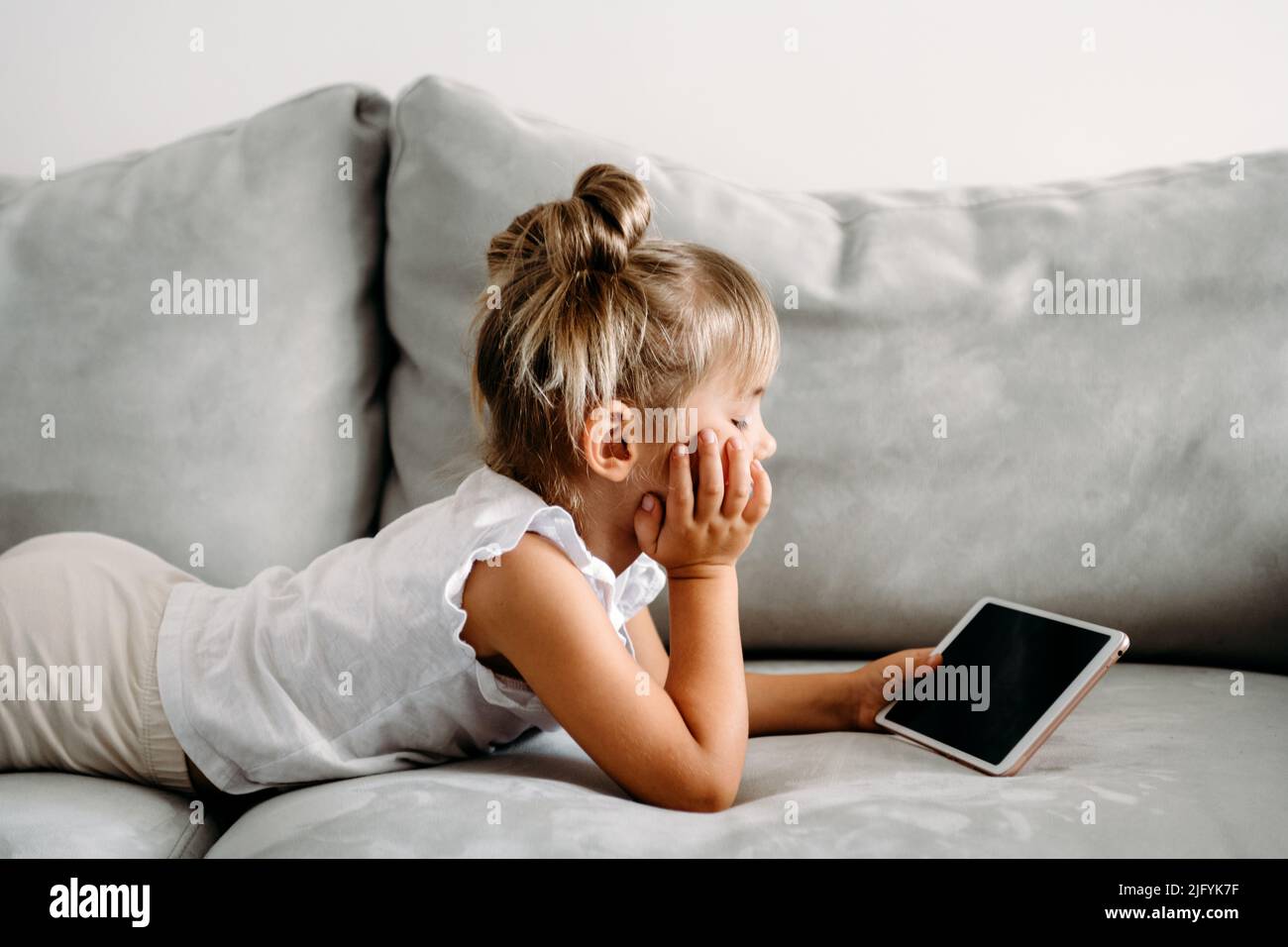 Toddler girl playing with digital wireless tablet computer on couch at ...