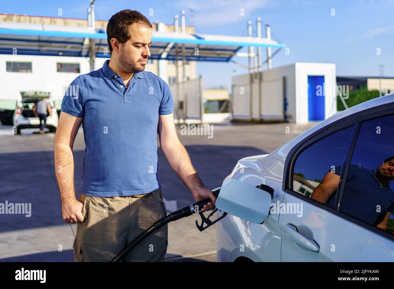 Caucasian young man refilling the tank of a fuel car at a gas station ...