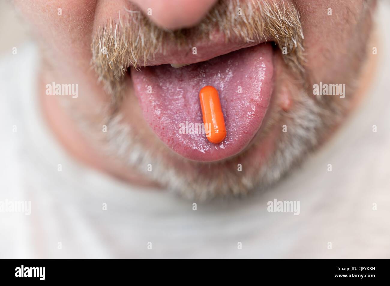 A man takes medication. The lower part of the man's face. Orange pill ...