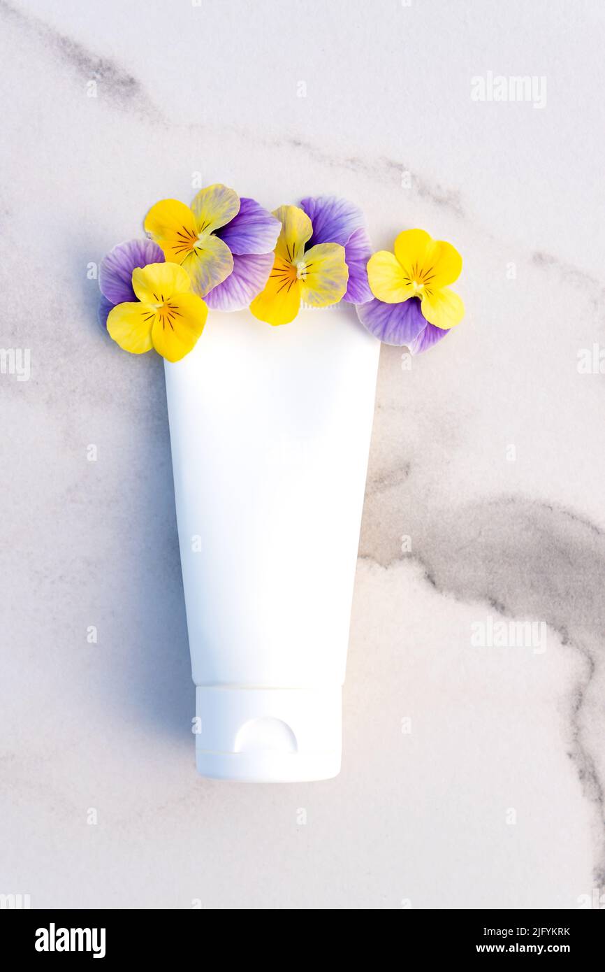 White tube with cosmetic product with pansy flowers on marble ...