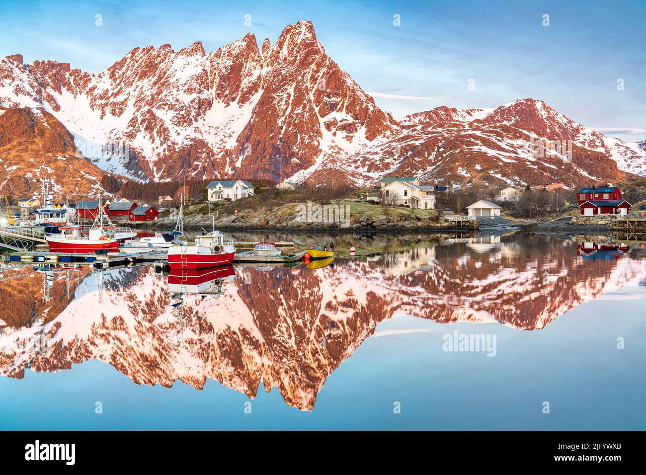 Fishing boats and snowcapped mountains mirrored in the fjord at sunrise ...