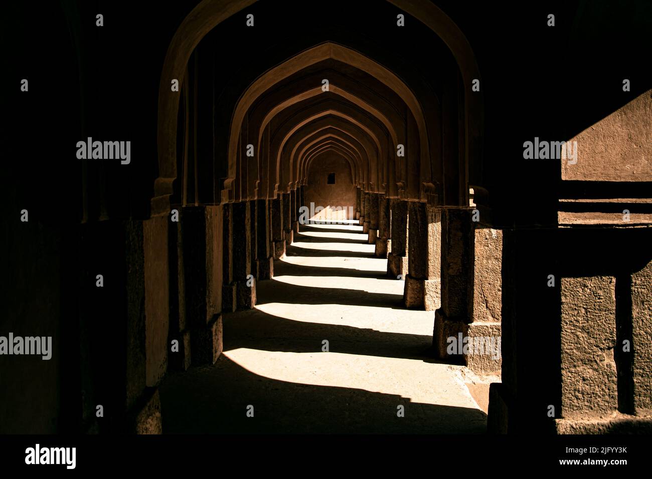 A beautiful shot of a dark arcade corridor with columns in sunlight in ...