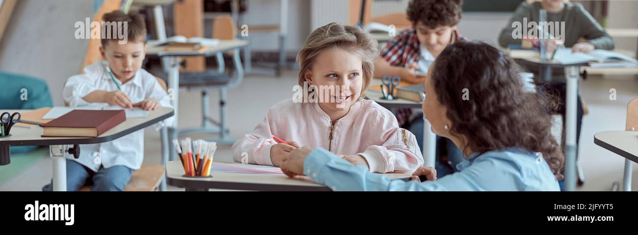 Happy kind teacher is helping kids in elementary school lessons Stock ...