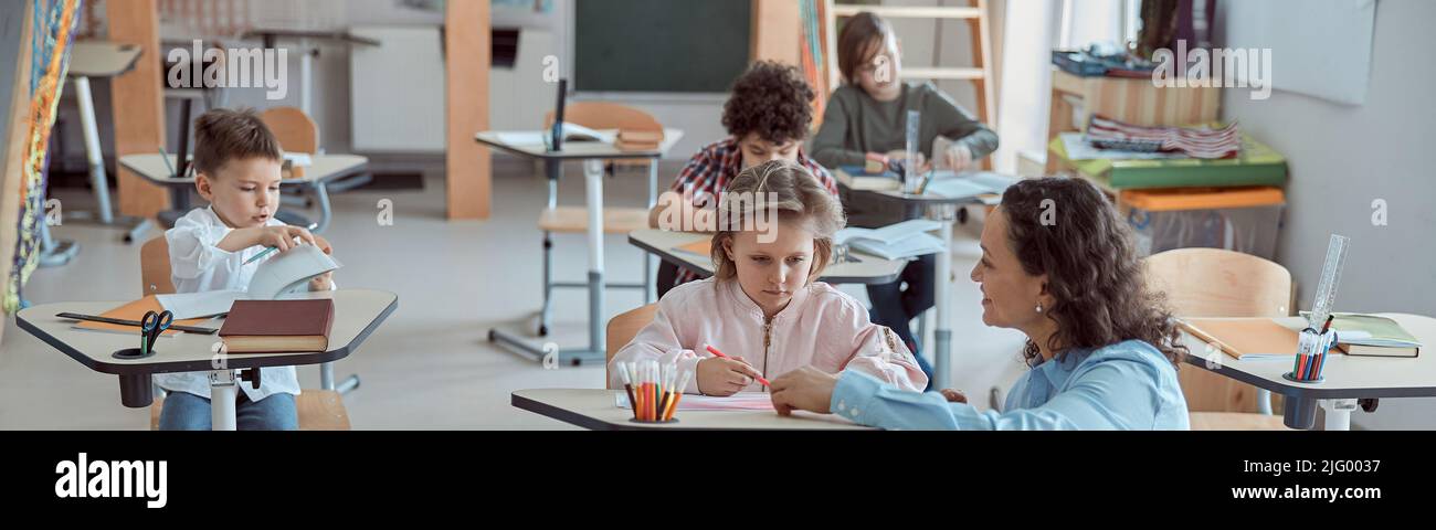 Happy kind teacher is helping kids in elementary school lessons Stock ...