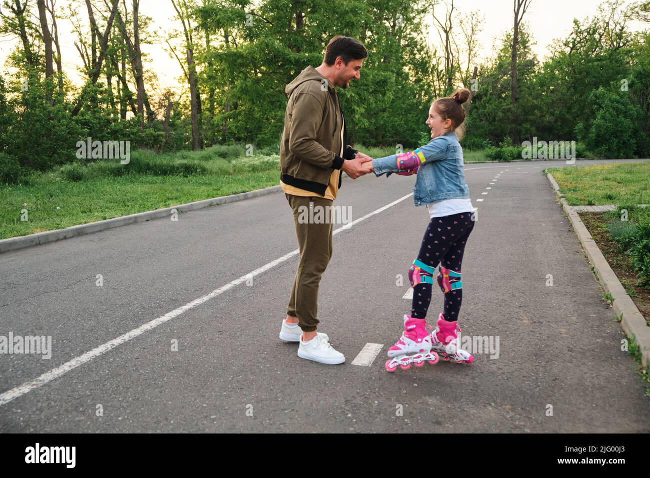 A father teaching his daughter roller skating in a park on summer day ...