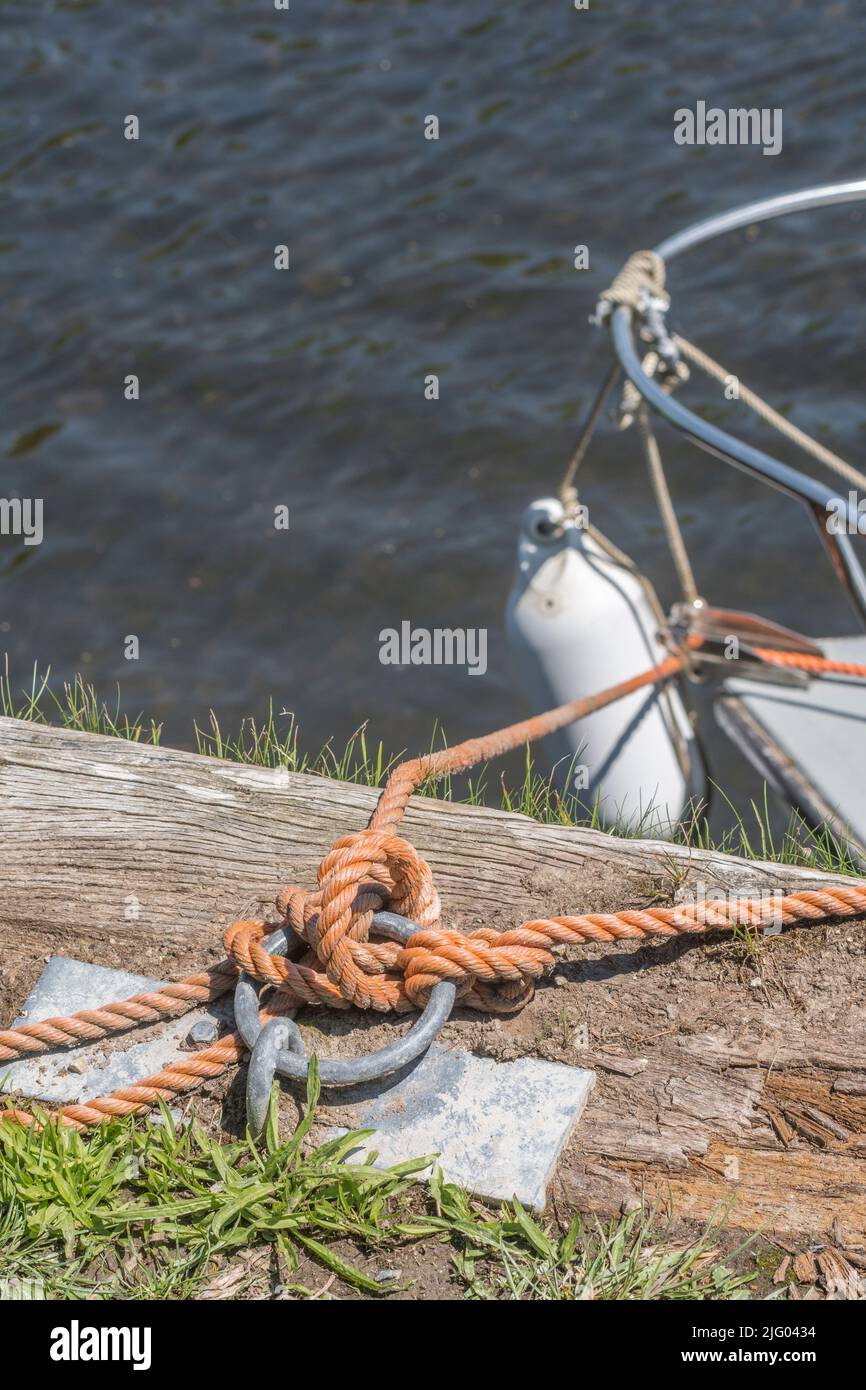 Sunny quayside with boat mooring rope attached to metal mooring ring ...