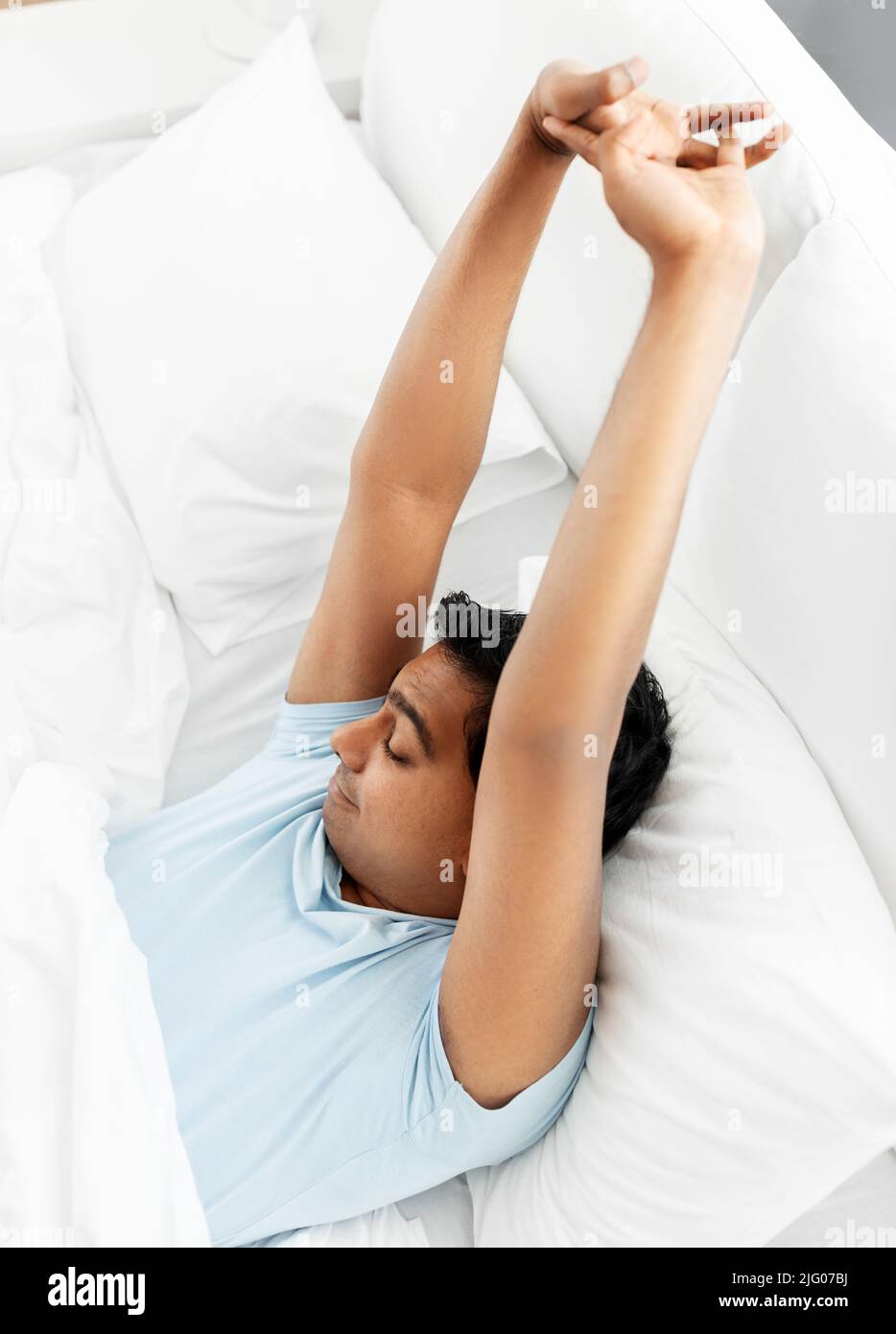 sleepy indian man stretching in bed at home Stock Photo - Alamy