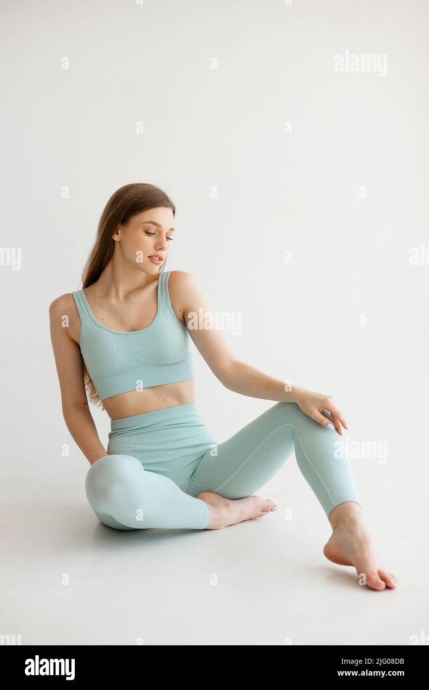 Beautiful athletic girl in a blue fitness suit sits on a white ...