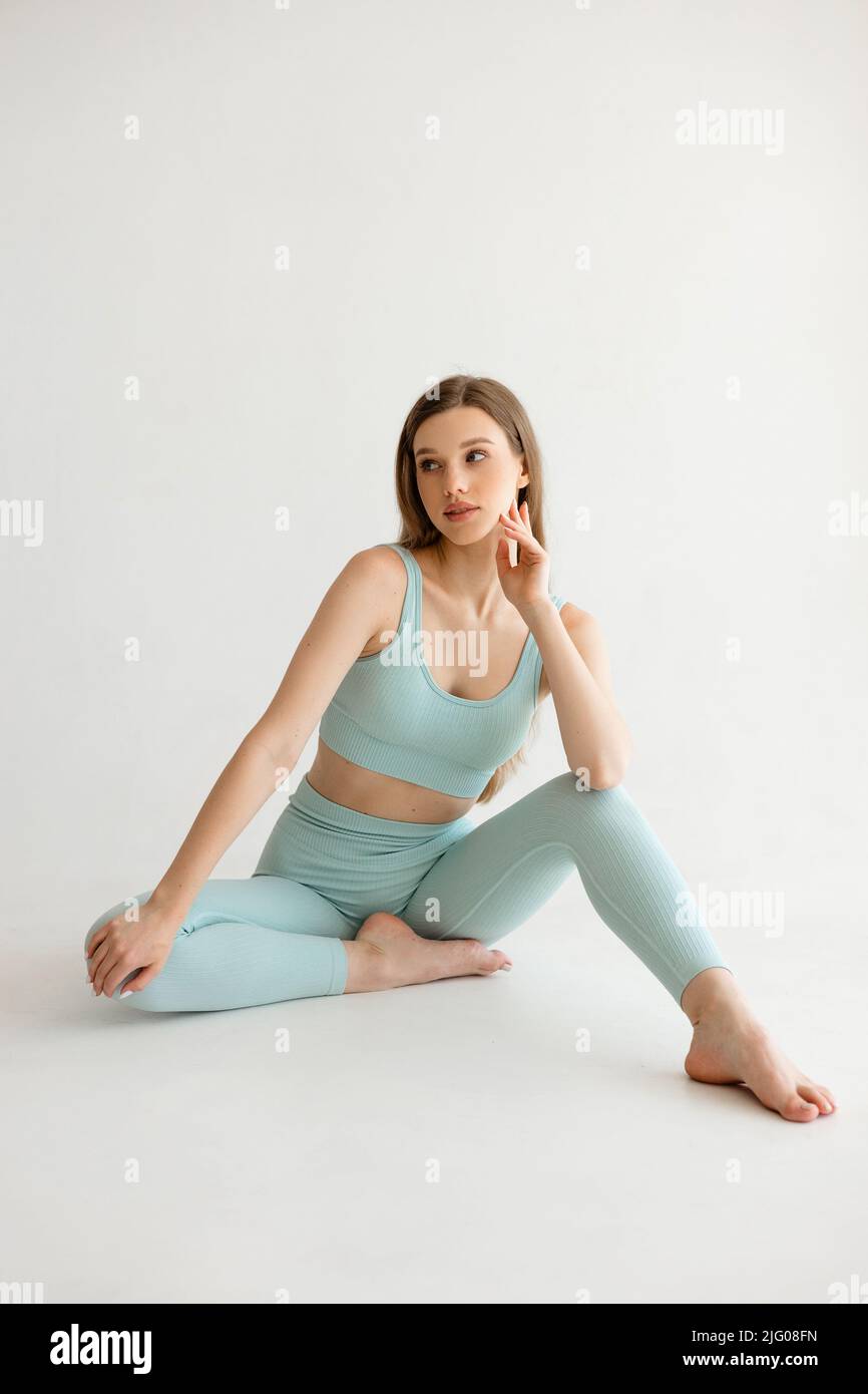 Beautiful athletic girl in a blue fitness suit sits on a white ...