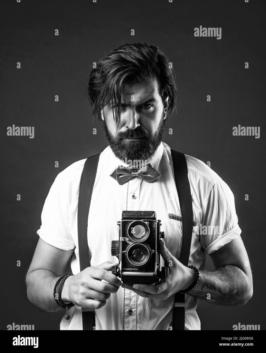 handsome mature man in suspenders holding retro camera while standing ...