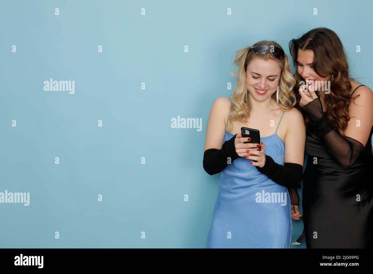 two young beautiful women, laughing and looking into their mobile ...