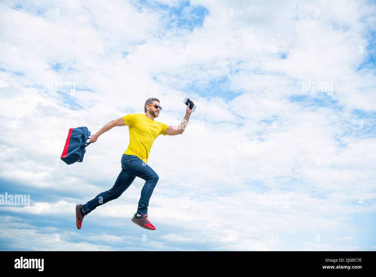 Energetic guy running with travel bag midair sky background, copy space ...