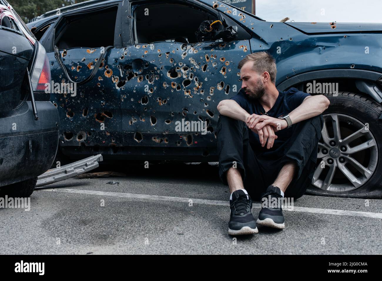 Man sits near shot damaged car riddled with bullets. Car shot by the ...