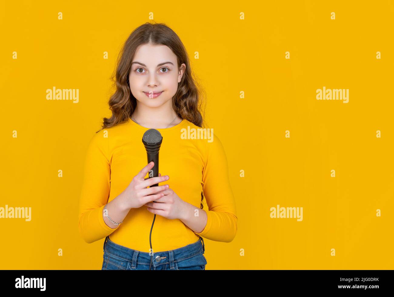 cheerful teen girl with microphone on yellow background. copy space ...