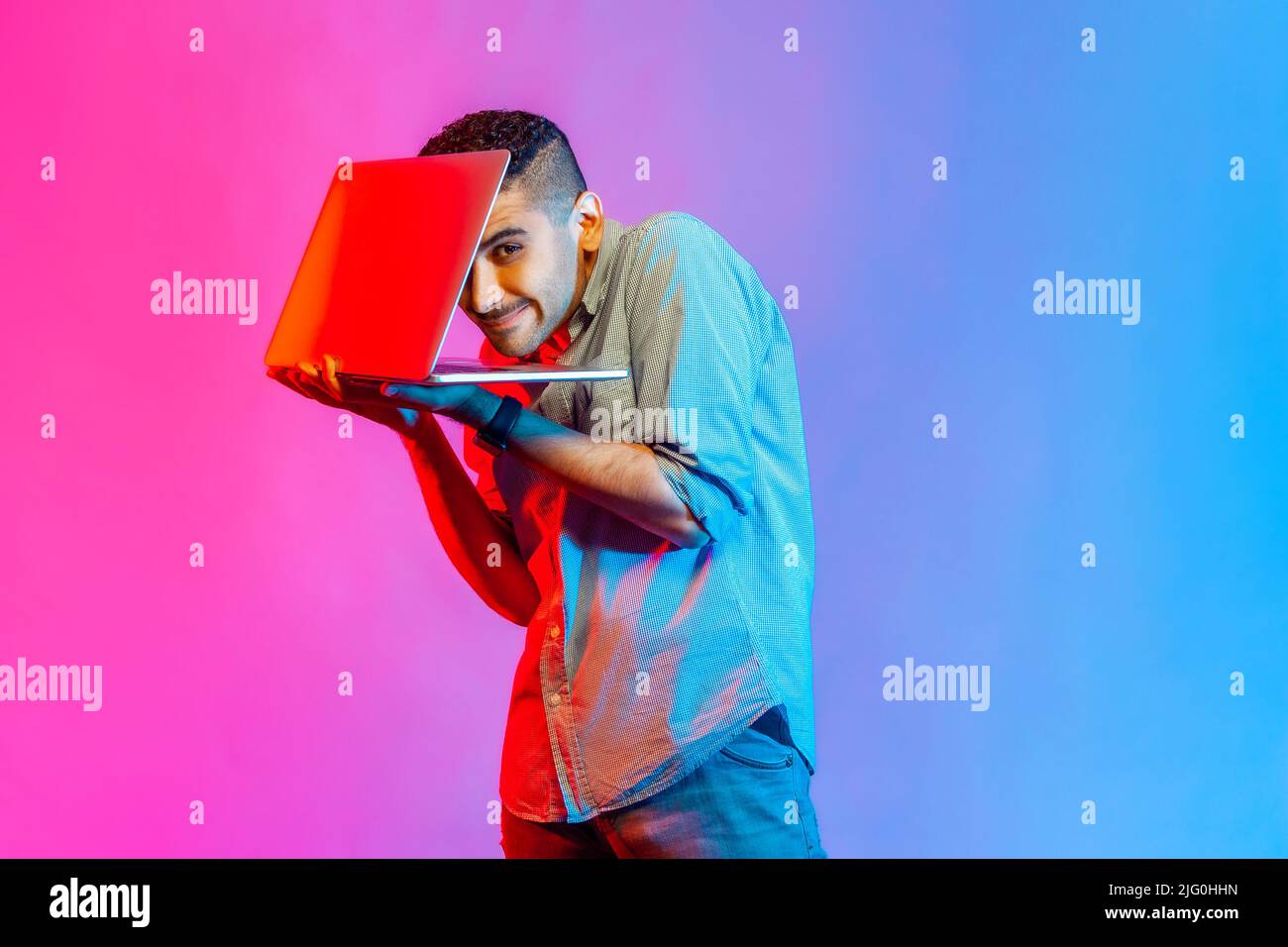 Portrait of funny young adult man in shirt holding laptop and looking ...