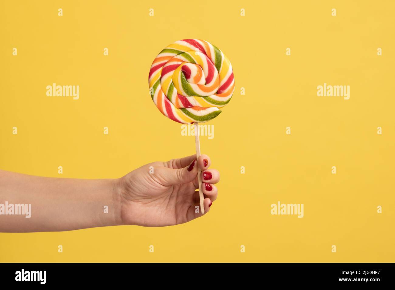 Closeup of woman hand holding appetizing round rainbow candy on stick ...