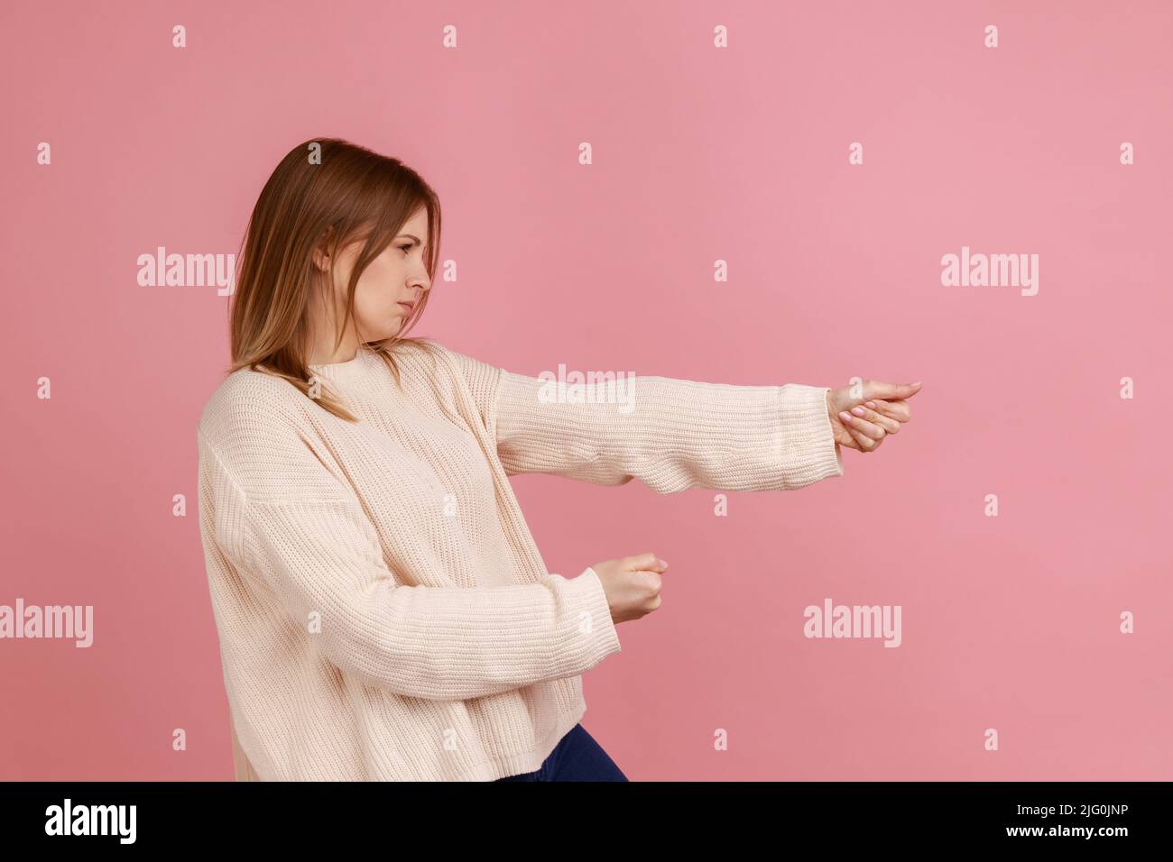 Portrait of blond woman striving hard to pull invisible rope, holding ...
