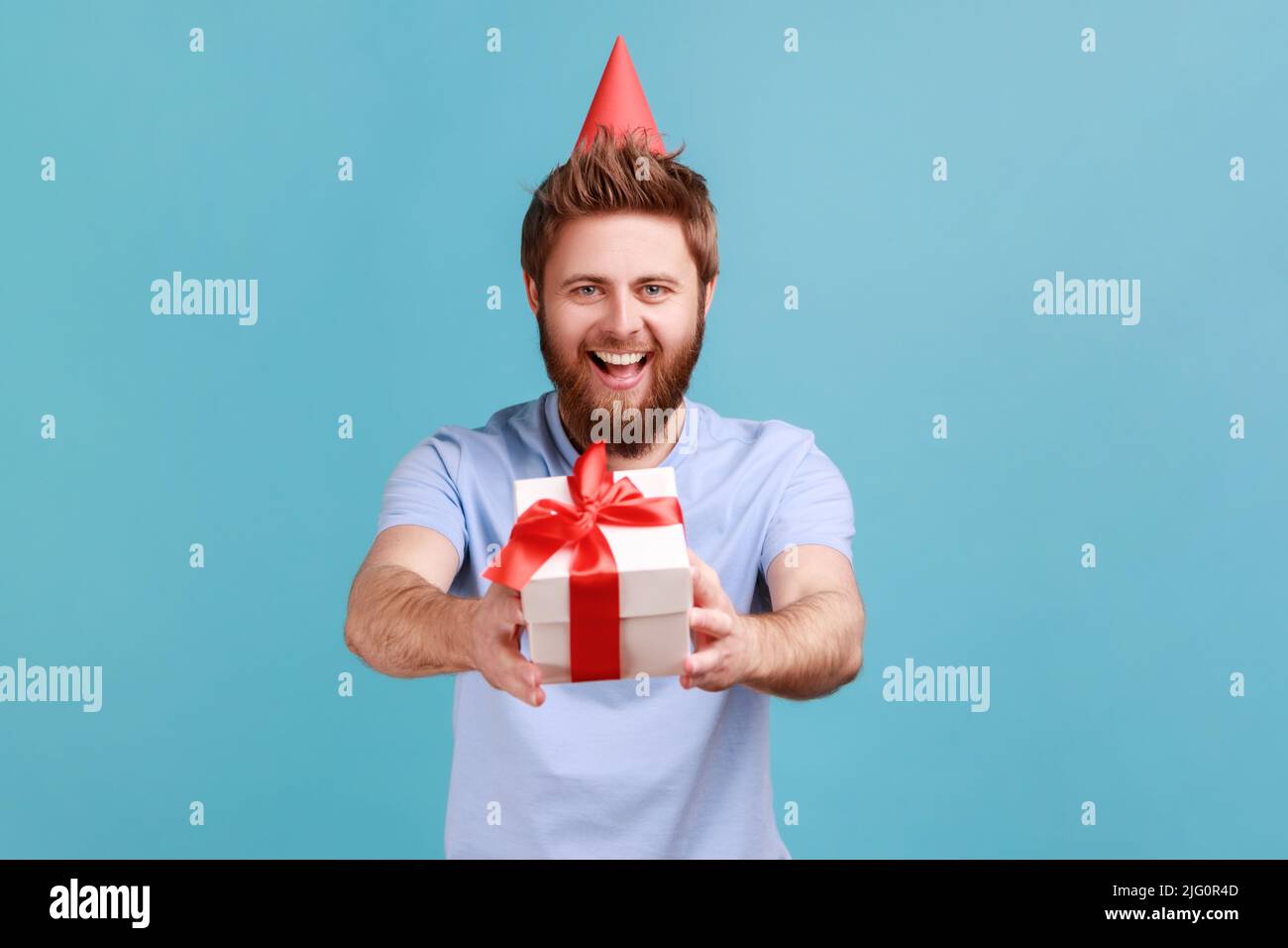 Portrait of man in party cone giving birthday gift and smiling, sharing ...