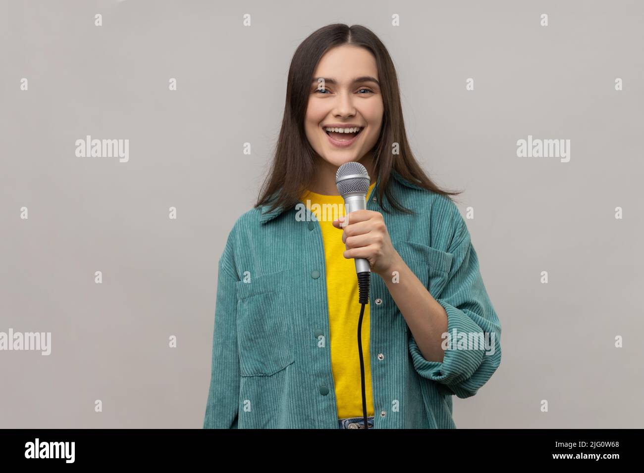 Portrait of positive woman reporter standing with microphone in hands ...