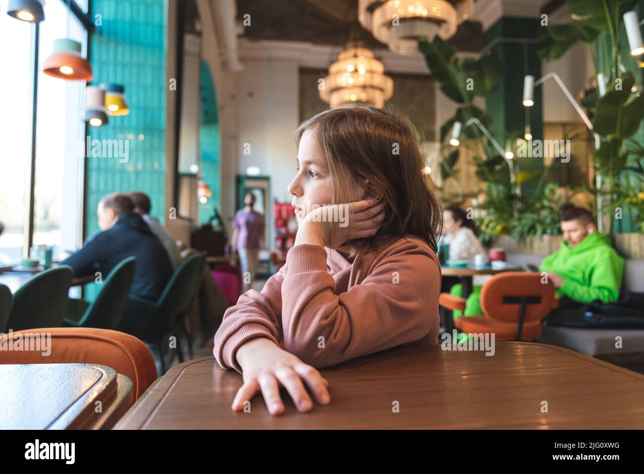 a cute brooding girl sits at a table in a cafe and looks out the window ...