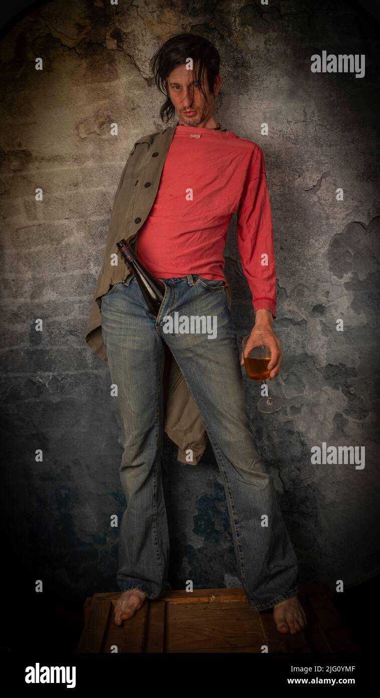 Junkie man with black hair and bottle with joint near old stone wall ...