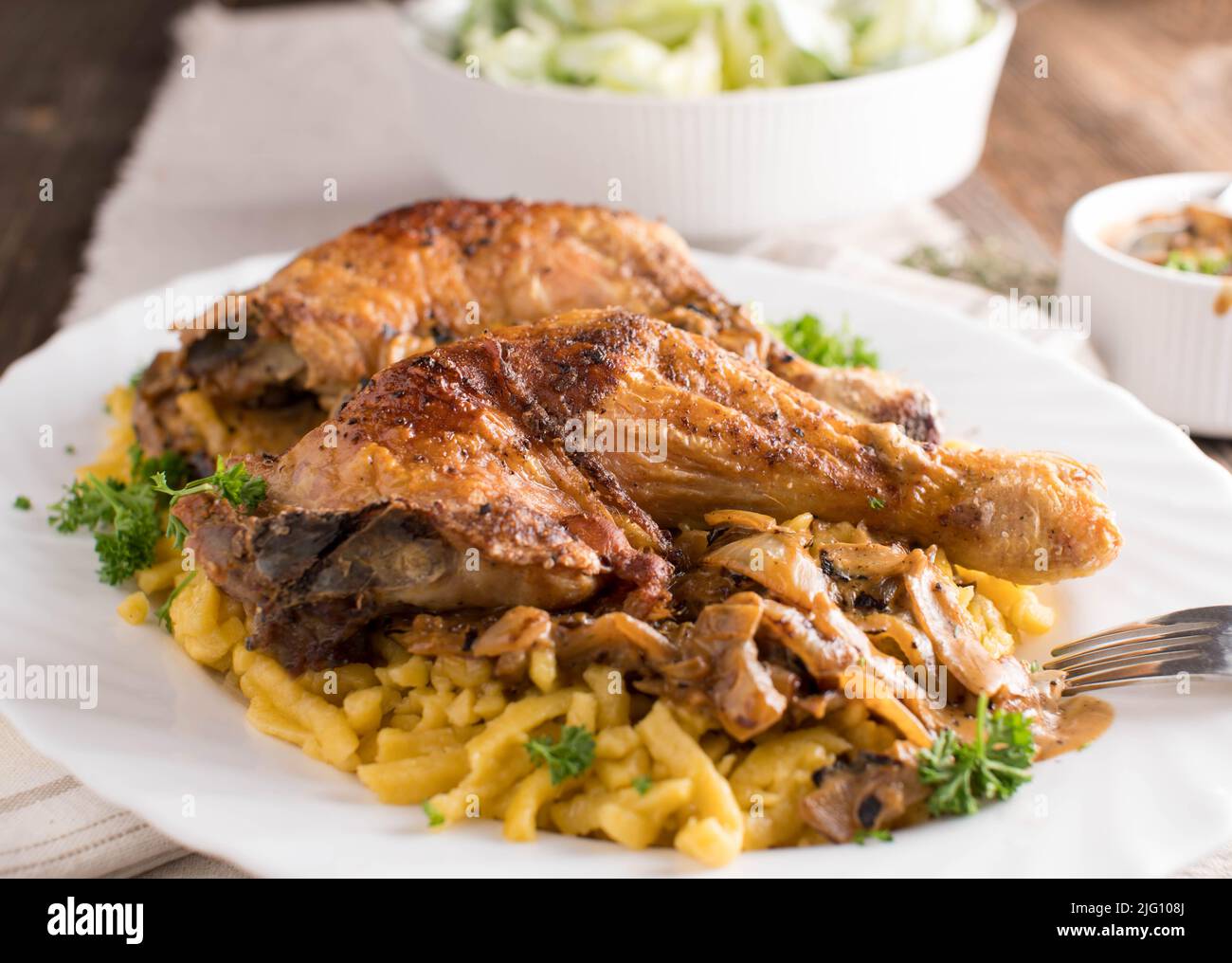 Spaetzle noodles with creamy onion sauce and roasted chicken legs on a ...