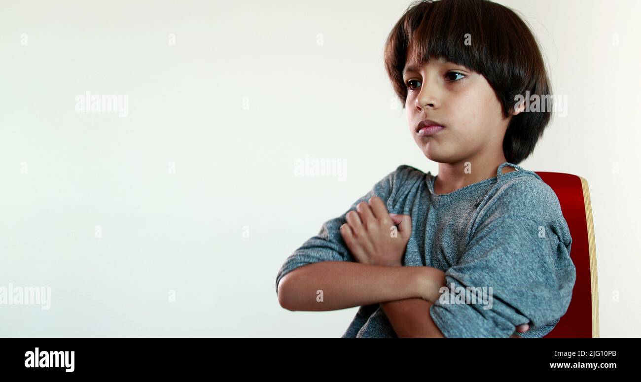 Pensive child boy sitting on chair thinking, kid crossing arms feeling ...