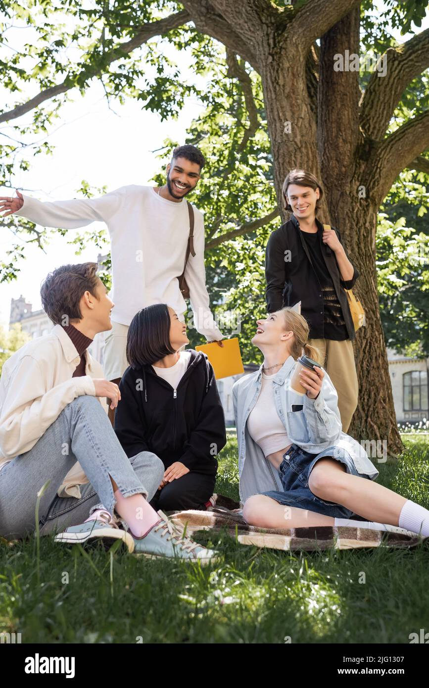 Positive interracial students with backpacks looking at friends on ...