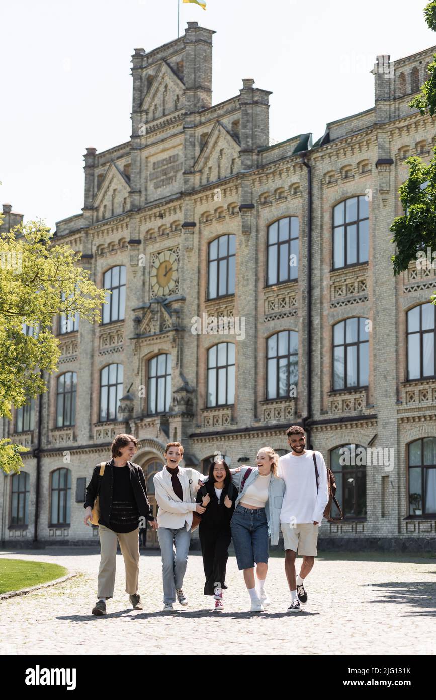 Smiling interracial students with backpacks walking near university ...