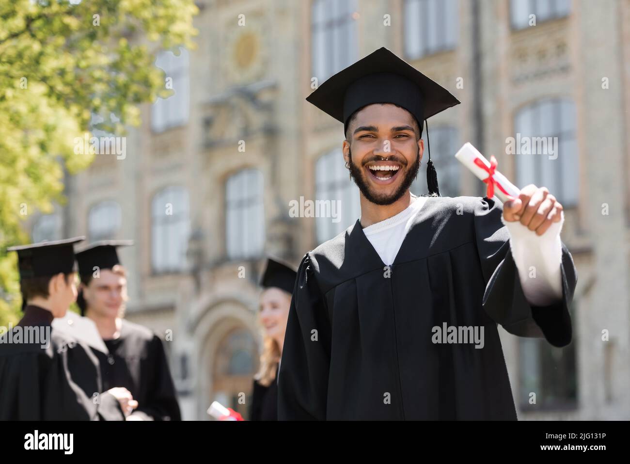 Happy african american bachelor in gown holding diploma outdoors Stock ...