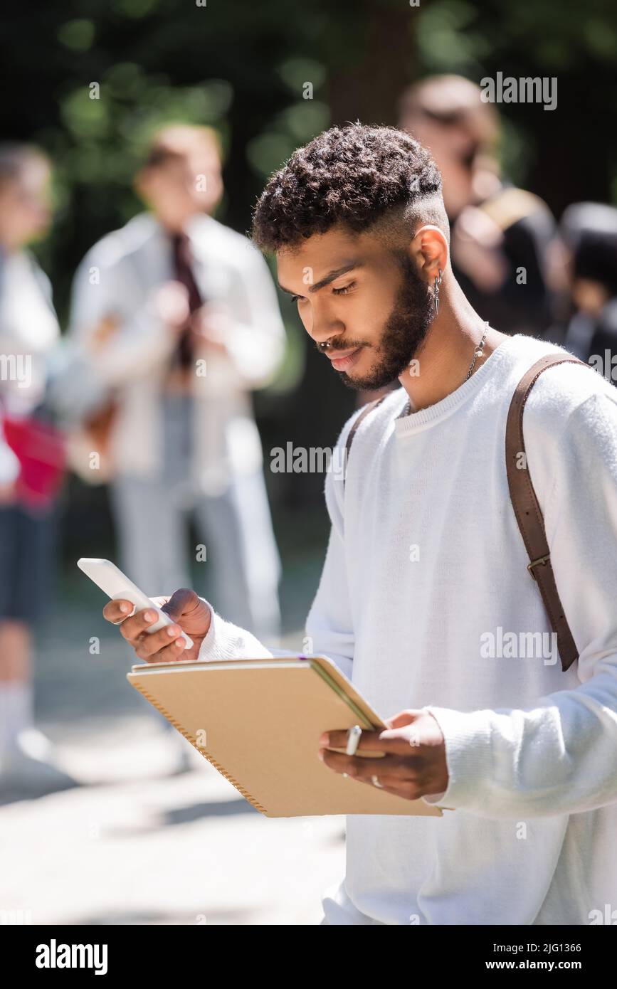 African american student holding smartphone and notebook in park Stock ...