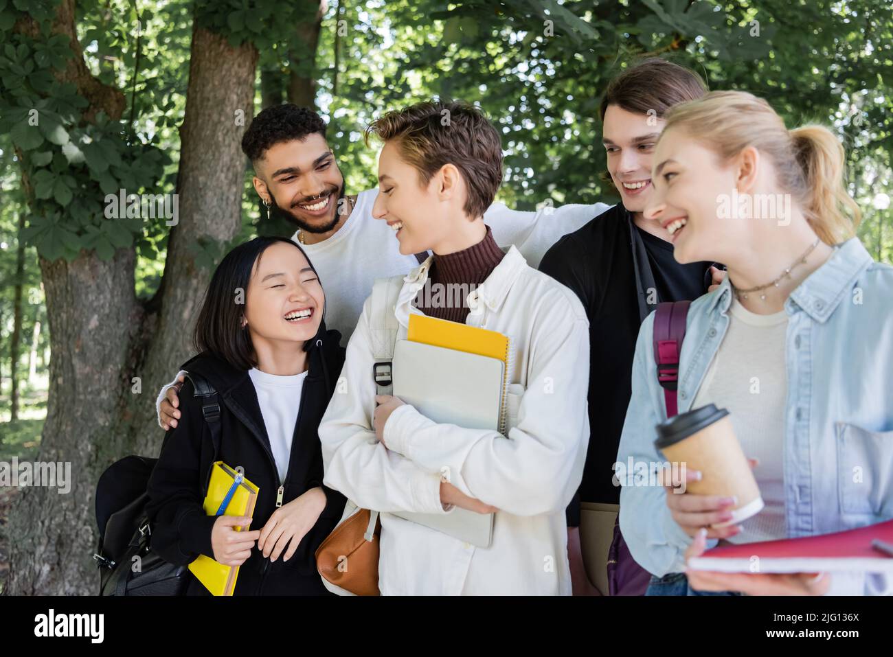 Cheerful multicultural students with copy books talking in park Stock ...