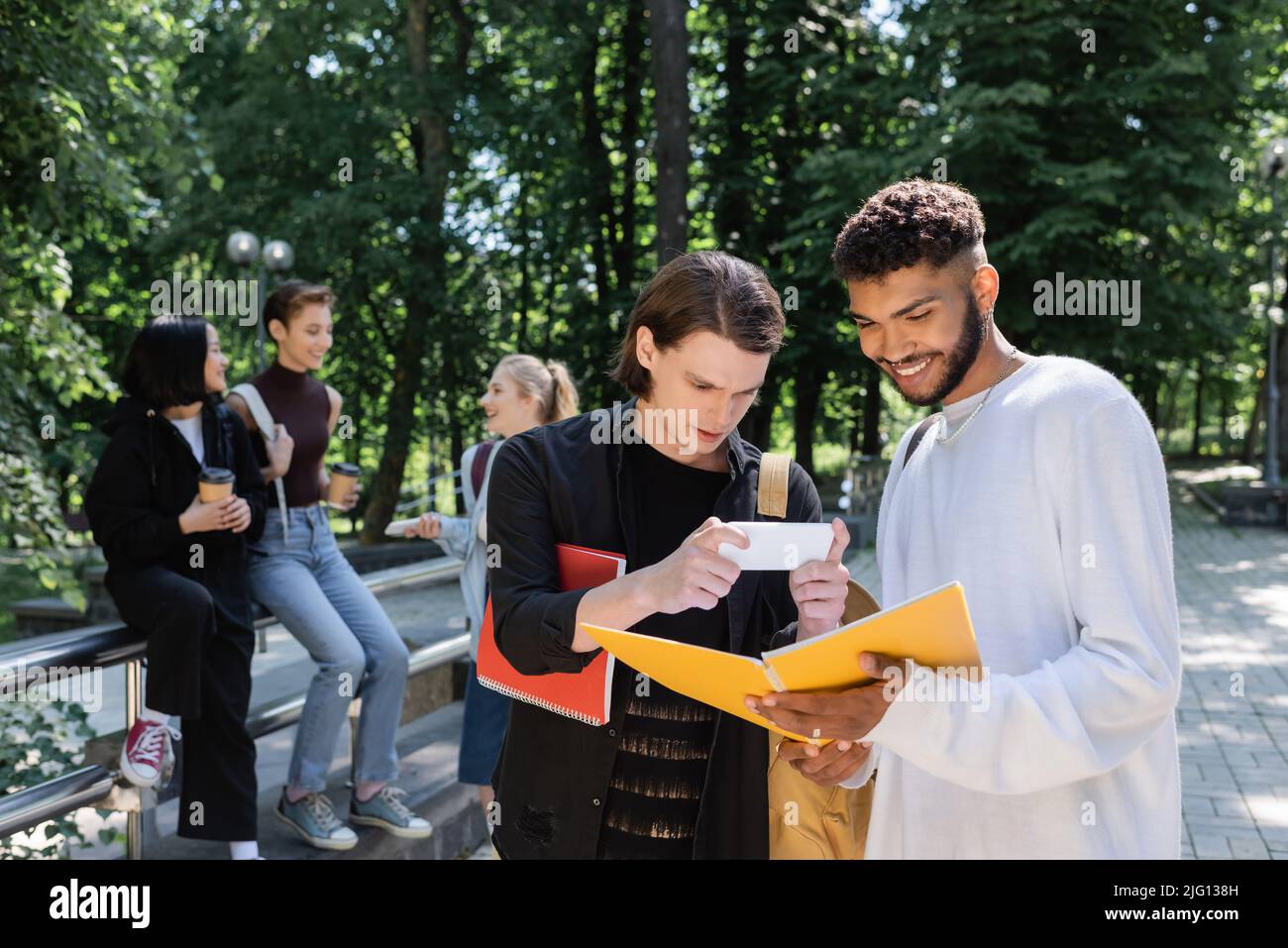 Smiling african american student holding notebook while friend taking ...