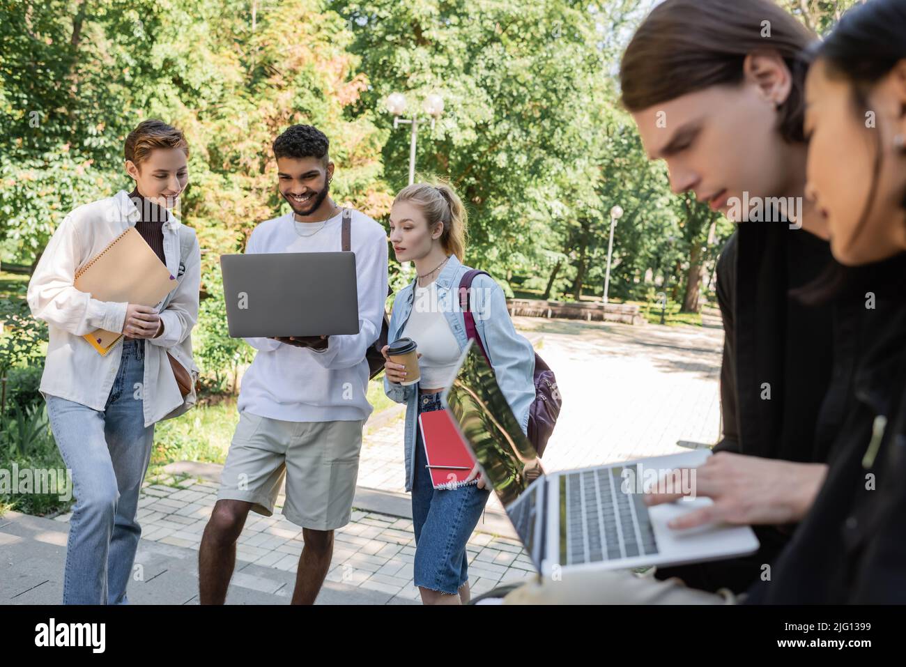 African american student holding laptop near friends with notebooks in ...
