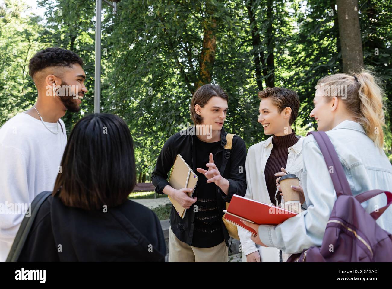 Students with backpacks talking near multicultural friends in park ...
