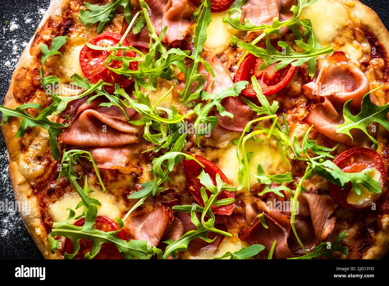 Traditional italian pizza with ham, cheese, tomatoes and arugula on ...