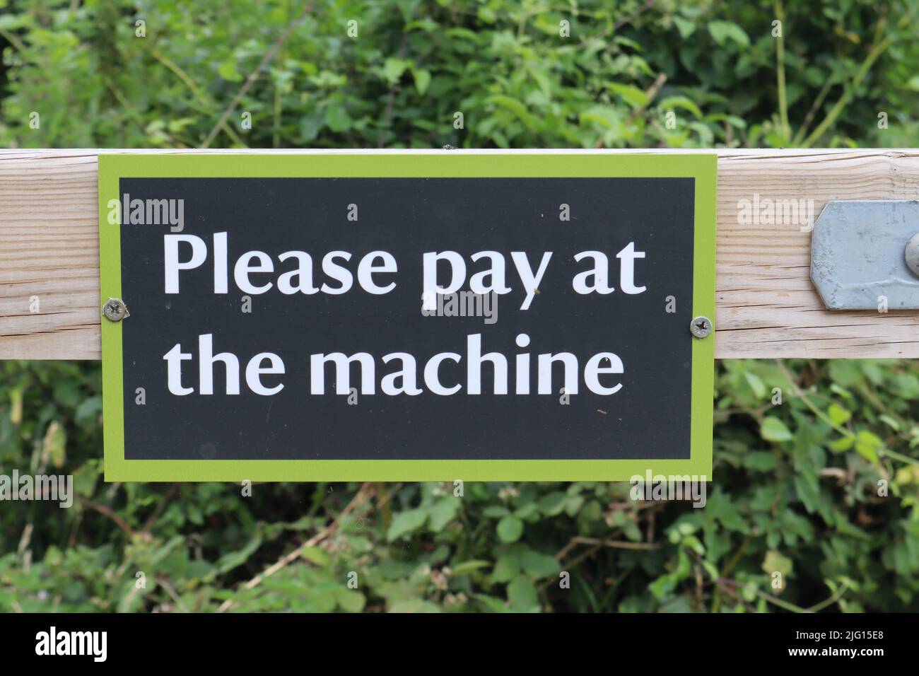 Black and white sign with a green border saying Pleas pay at machine ...