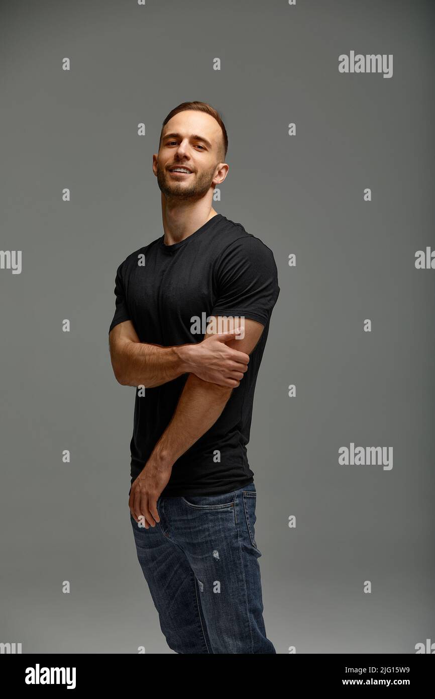 An attractive white man in jeans and black shirts tands in half growth ...