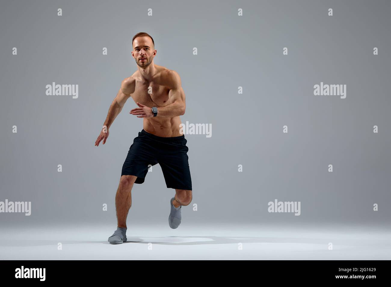 Developing endurance. Male athlete in motion isolated over gray studio ...