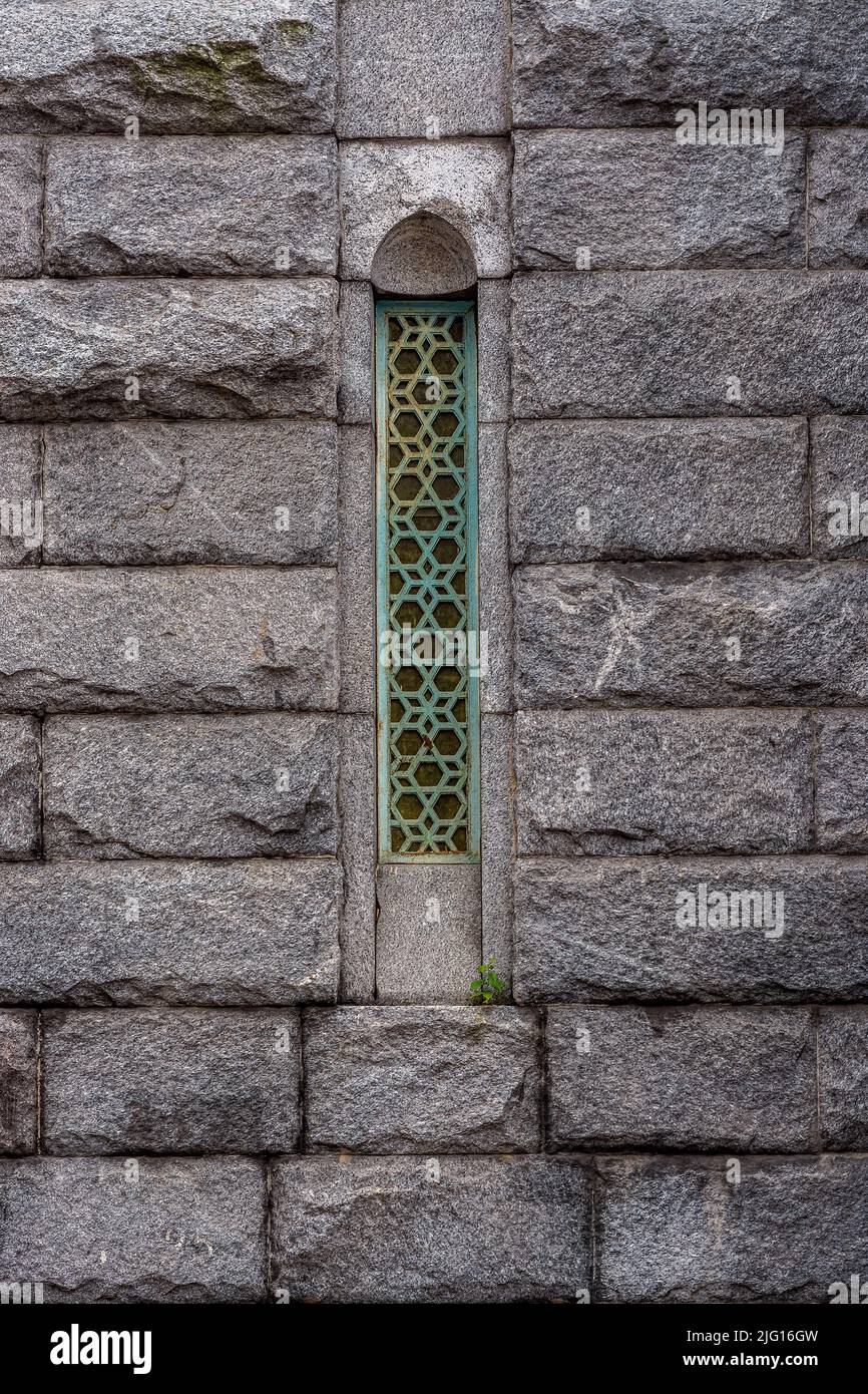 Narrow window with a green iron grate in a niche of an old gray stone ...