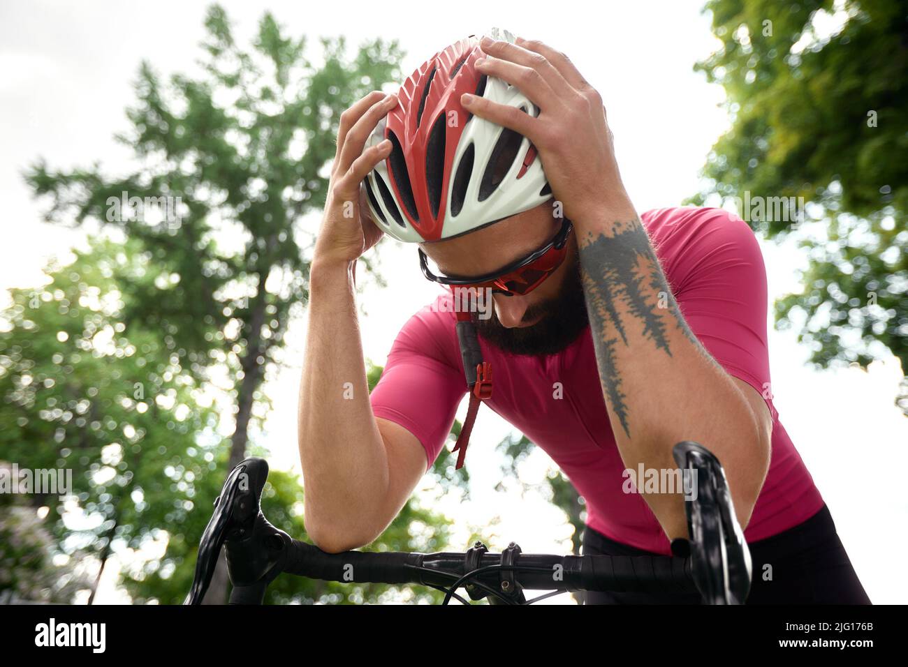 Tired male cyclist in sportswear, glasses and protective helmet walking ...