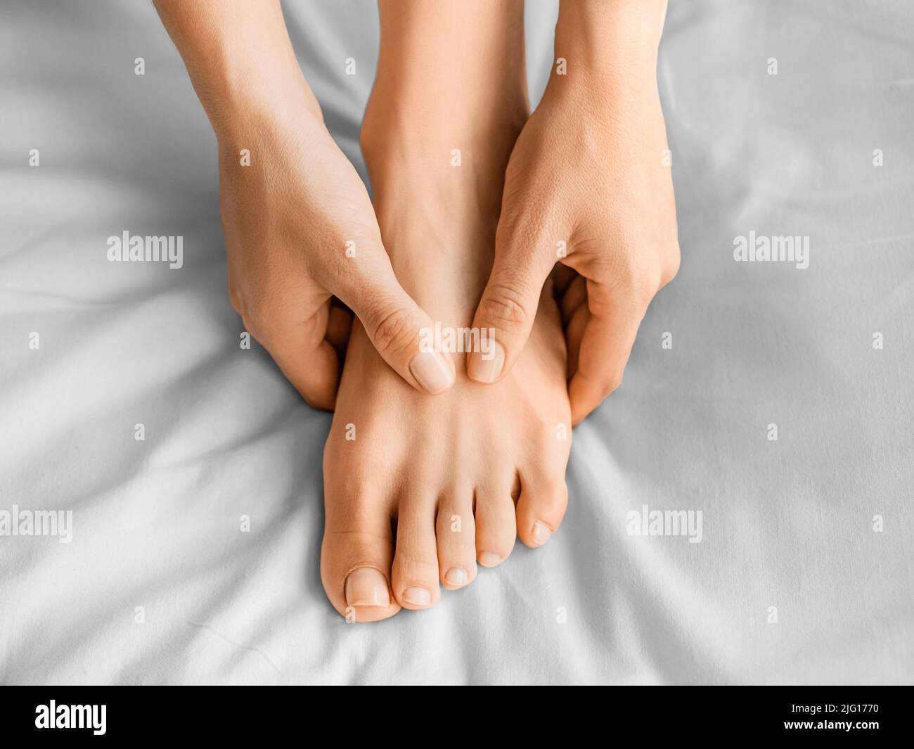 A Woman Massages Her Foot While Sitting In Bed Close Up View Stock