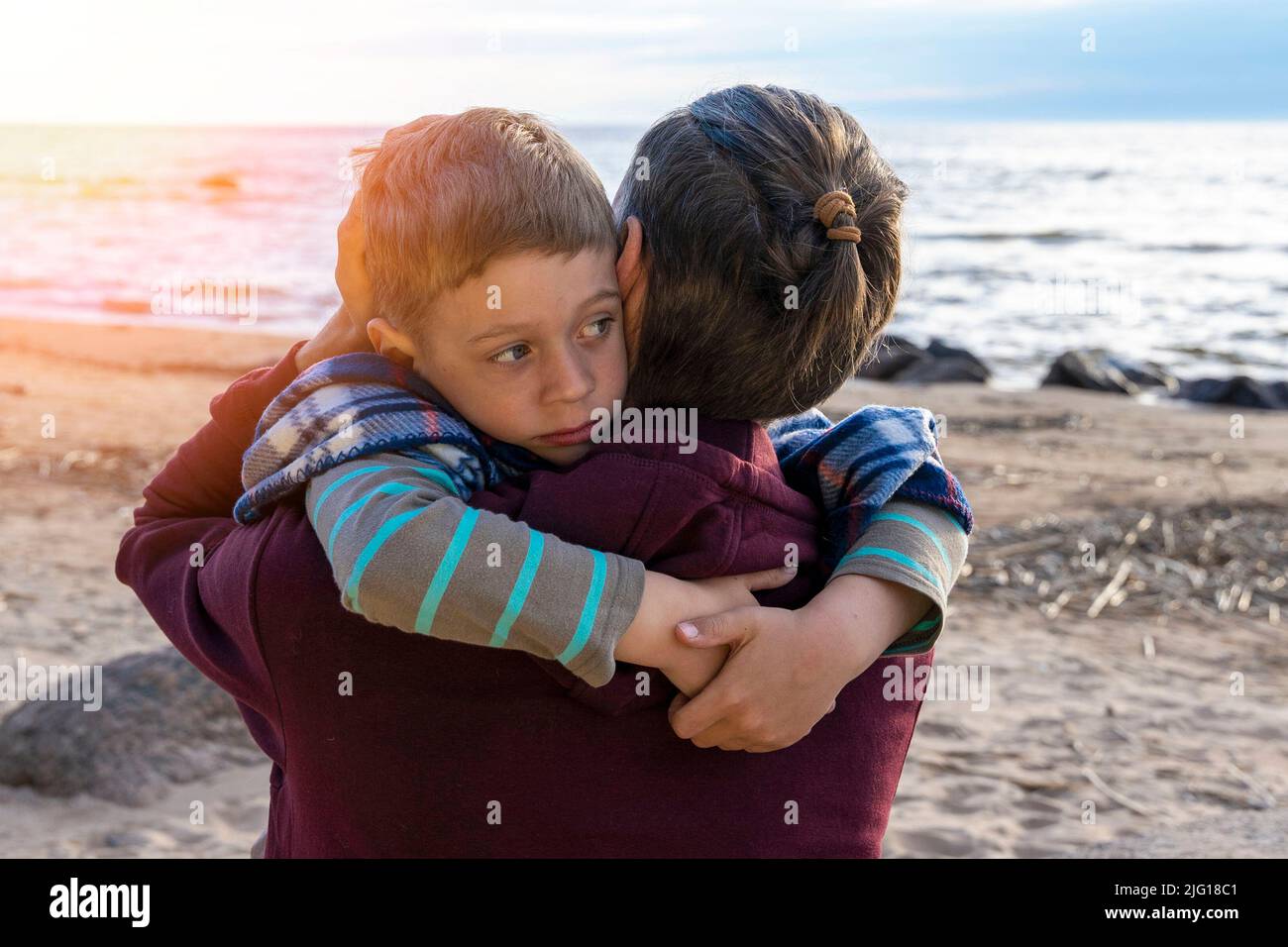 Cute sad preschool boy hugs his dad on the seashore in sunset light ...